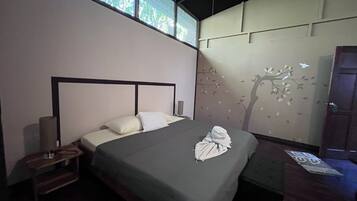 Um quarto com uma cama, mesa de cabeceira e prateleira na parede, além de uma porta.
