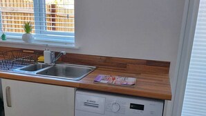 Cozinha compacta com máquina de lavar embutida, pia e janela com persianas.
