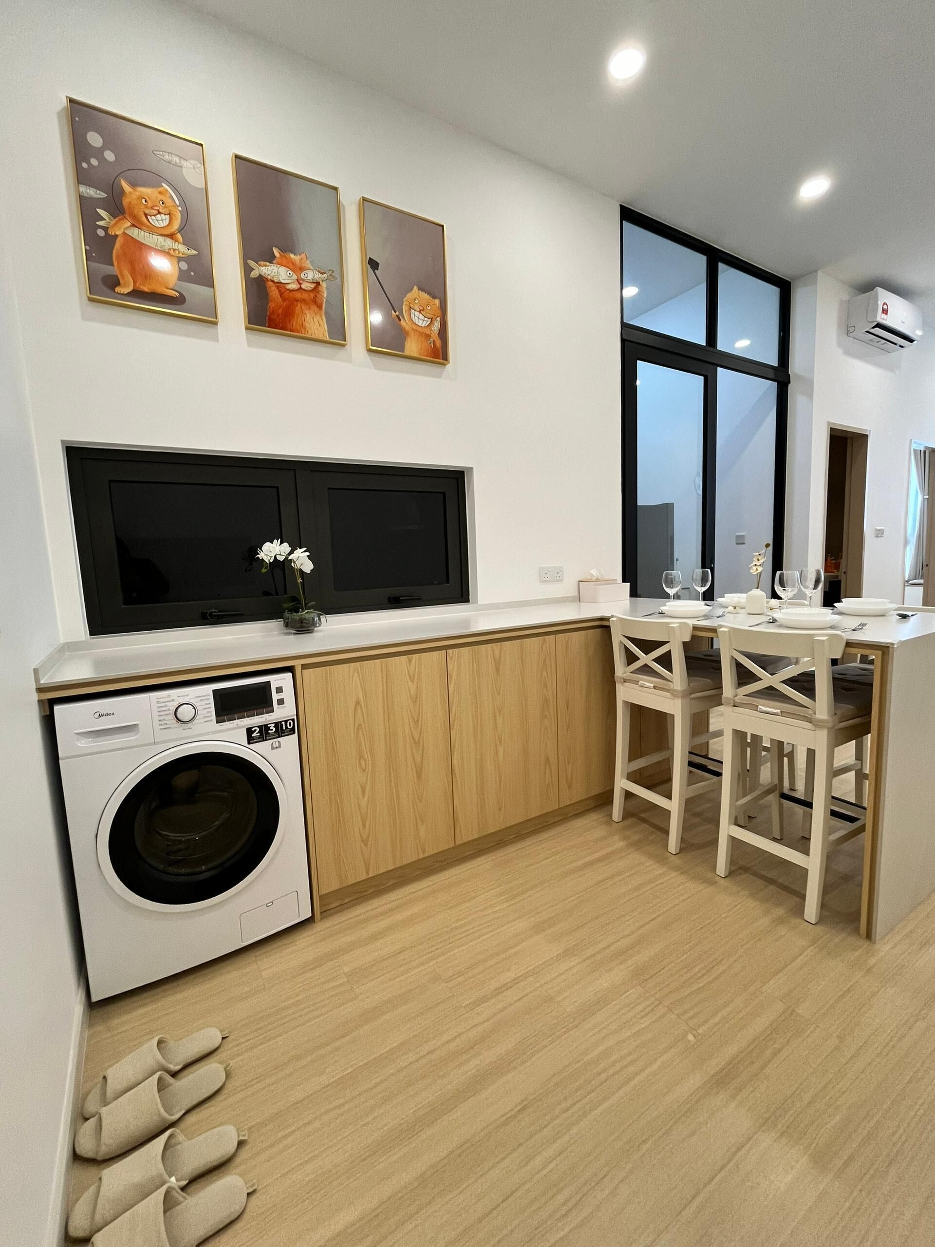 Uma cozinha moderna com máquina de lavar embutida, área de refeições com mesa e cadeiras, e três obras de arte emolduradas na parede.