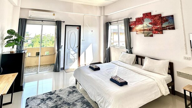 Quarto moderno com uma cama grande, uma escrivaninha, uma cadeira, uma planta em vaso e uma varanda com vista.