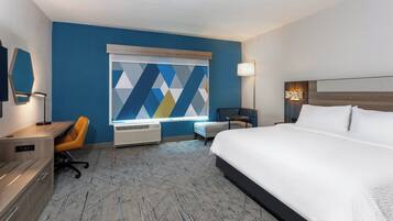 Quarto de hotel com uma cama grande, uma escrivaninha com cadeira, uma janela com vista geométrica e uma luminária fixada na parede.