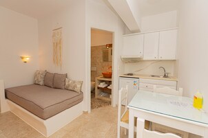 Quarto compacto com cama, pequeno espaço de cozinha e área de refeições.