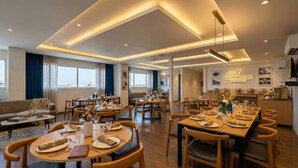 Um espaço de jantar de hotel com várias mesas preparadas para hóspedes, uma área de cozinha e vista para o aeroporto.