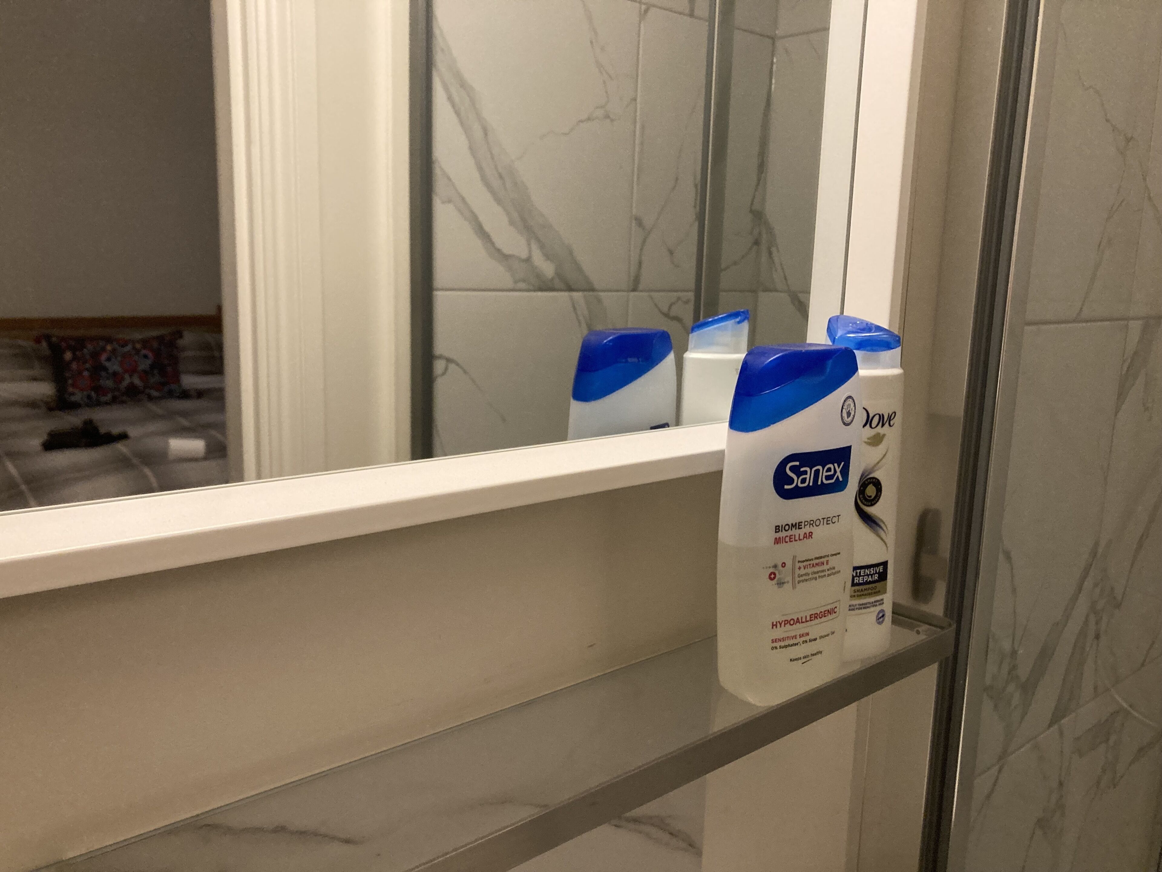 Um banheiro com pia branca, um espelho e uma embalagem de sabonete Sanex BiomeProtect Micellar na borda da pia.