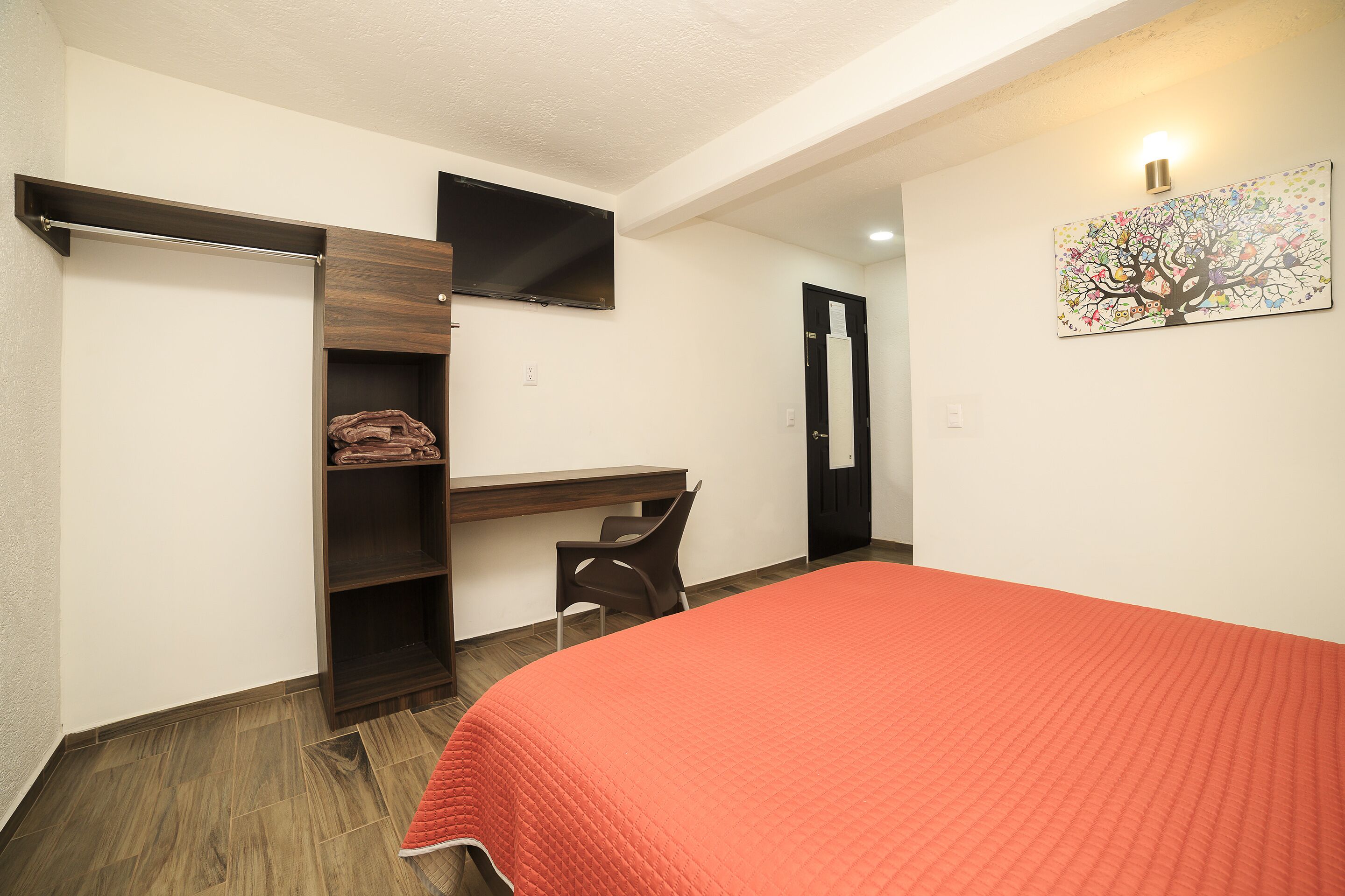 Um quarto com cama, escrivaninha, cadeira, televisão e guarda-roupa.