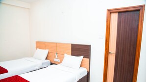 Quarto de hotel com duas camas de solteiro, cabeceira de madeira, porta de madeira e parede branca.