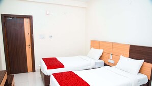 Quarto de hotel com duas camas, cabeceira de madeira, colcha vermelha e preta, roupa de cama branca e escrivaninha de madeira com uma cadeira.