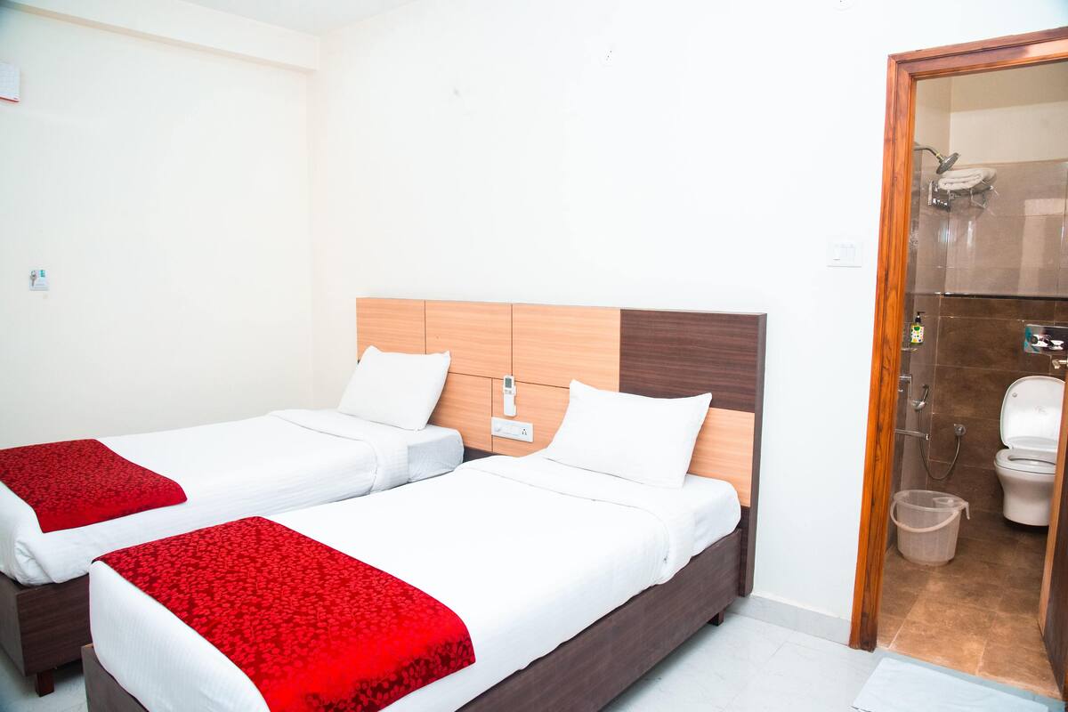 Quarto de hotel com duas camas, cabeceira de madeira, roupa de cama branca e manta vermelha.
