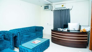 Quarto com sofá azul, balcão de recepção de madeira e ventoinha no teto.