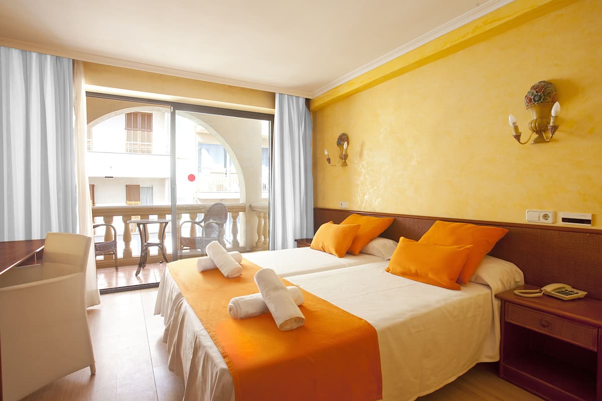 Quarto de hotel com duas camas, uma varanda, uma escrivaninha e uma mesa de cabeceira com telefone.