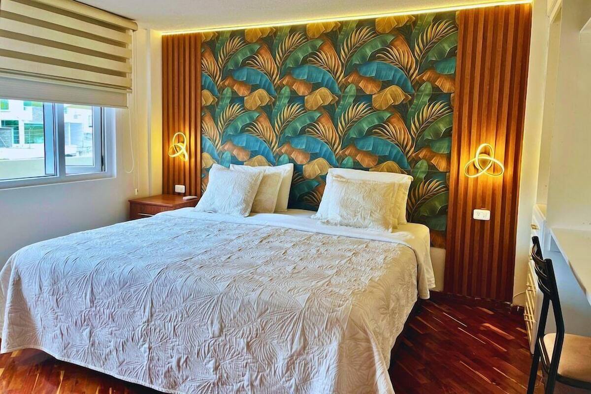 Quarto de hotel com uma cama grande, uma cabeceira estampada e duas luminárias de apoio.