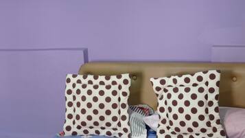 Cama com colcha xadrez, duas almofadas com bolinhas e cabeceira em parede roxa.