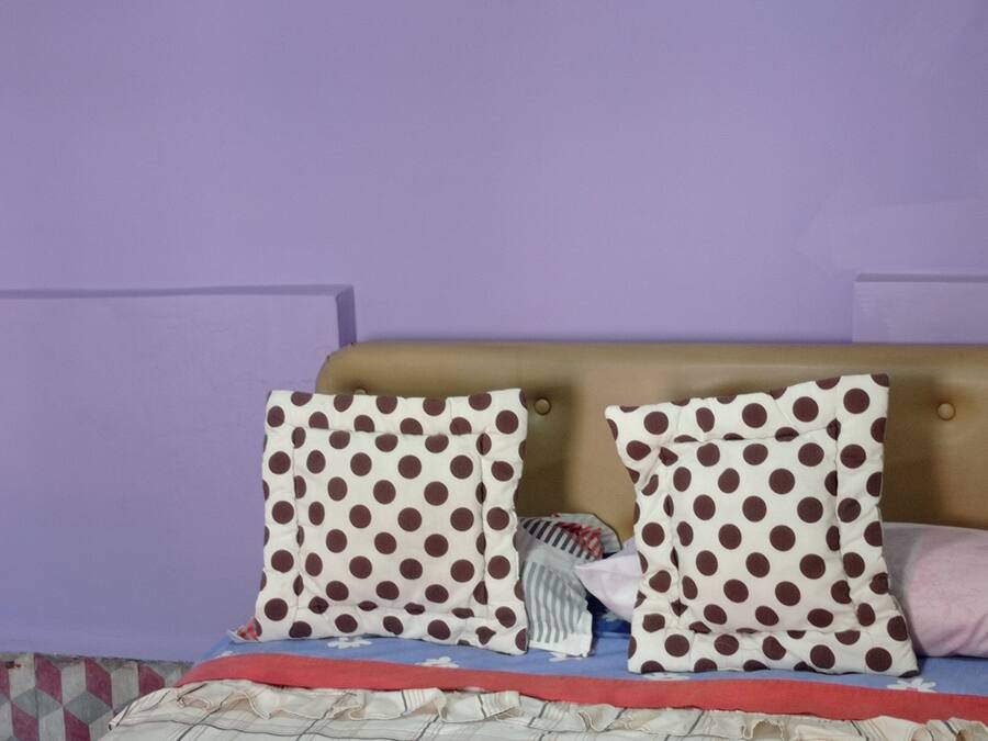 Cama com colcha xadrez, duas almofadas com bolinhas e cabeceira em parede roxa.