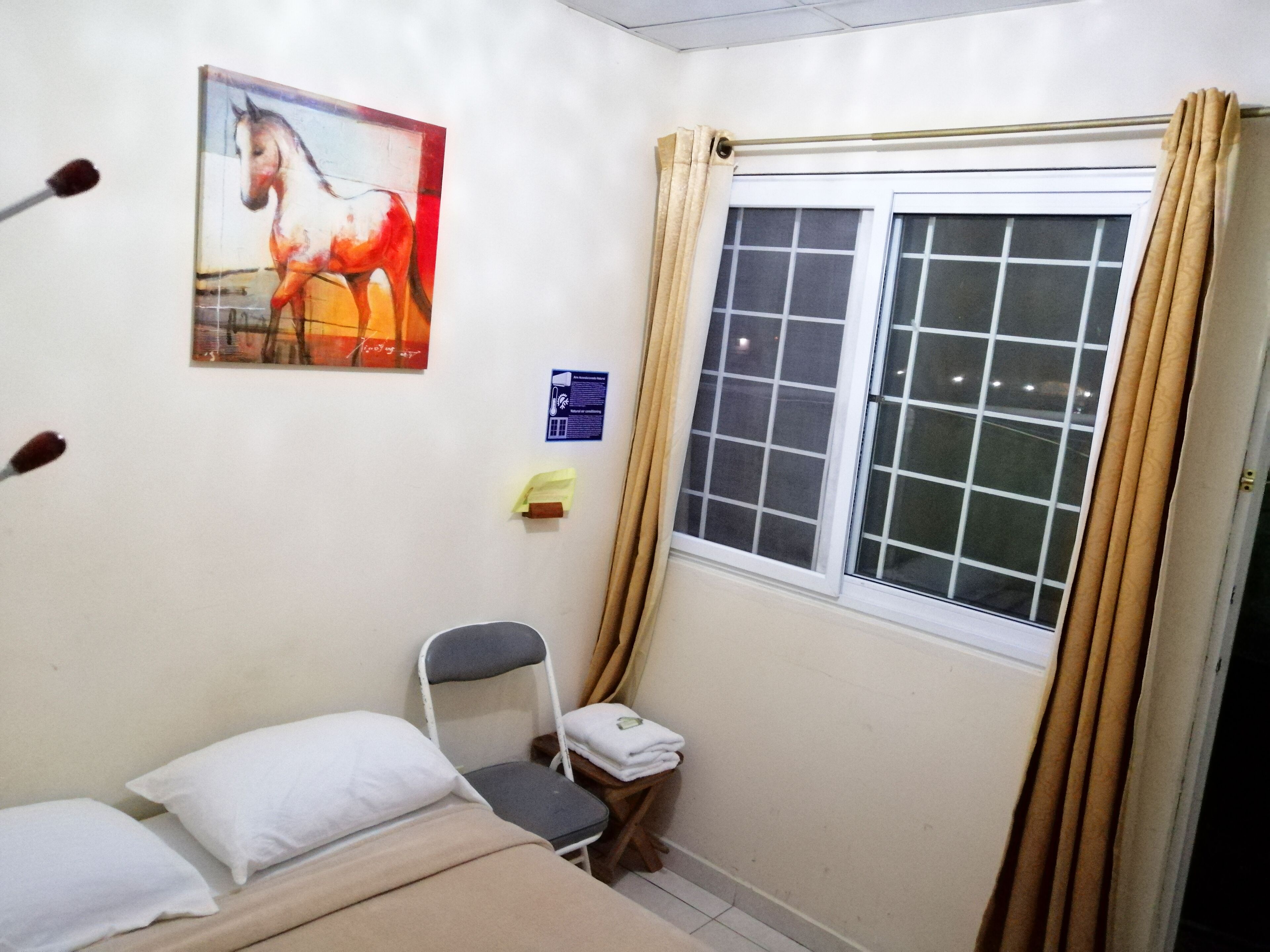 Quarto com uma cama, uma cadeira, uma janela com cortinas e um quadro na parede.