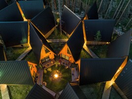 Um conjunto de cabanas modernas e angulares, com uma fogueira central rodeada por assentos.