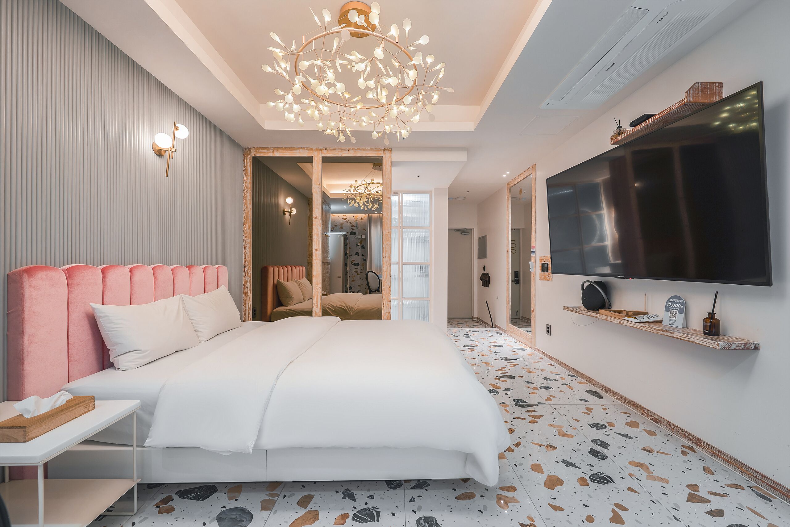 Quarto moderno com uma cama grande, televisão na parede e um candelabro singular.