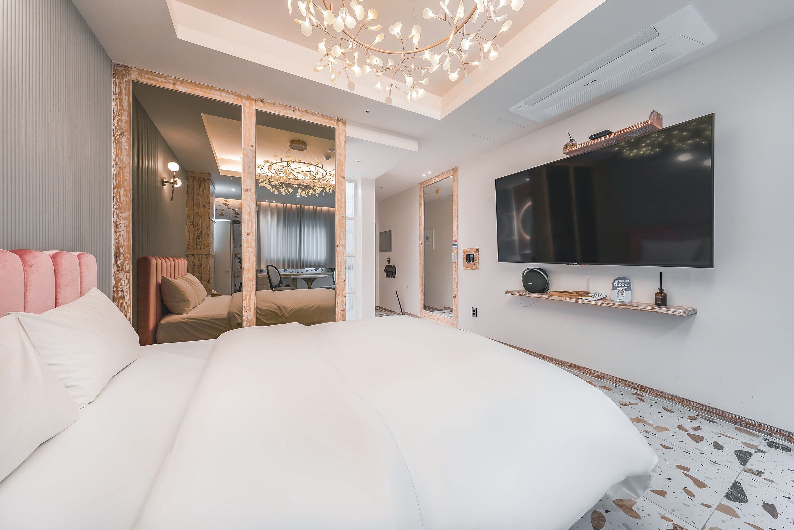 Quarto de hotel moderno com uma cama grande, televisão na parede e espelho com moldura de madeira.