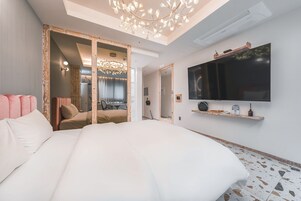 Quarto de hotel moderno com uma cama grande, televisão na parede e espelho com moldura de madeira.