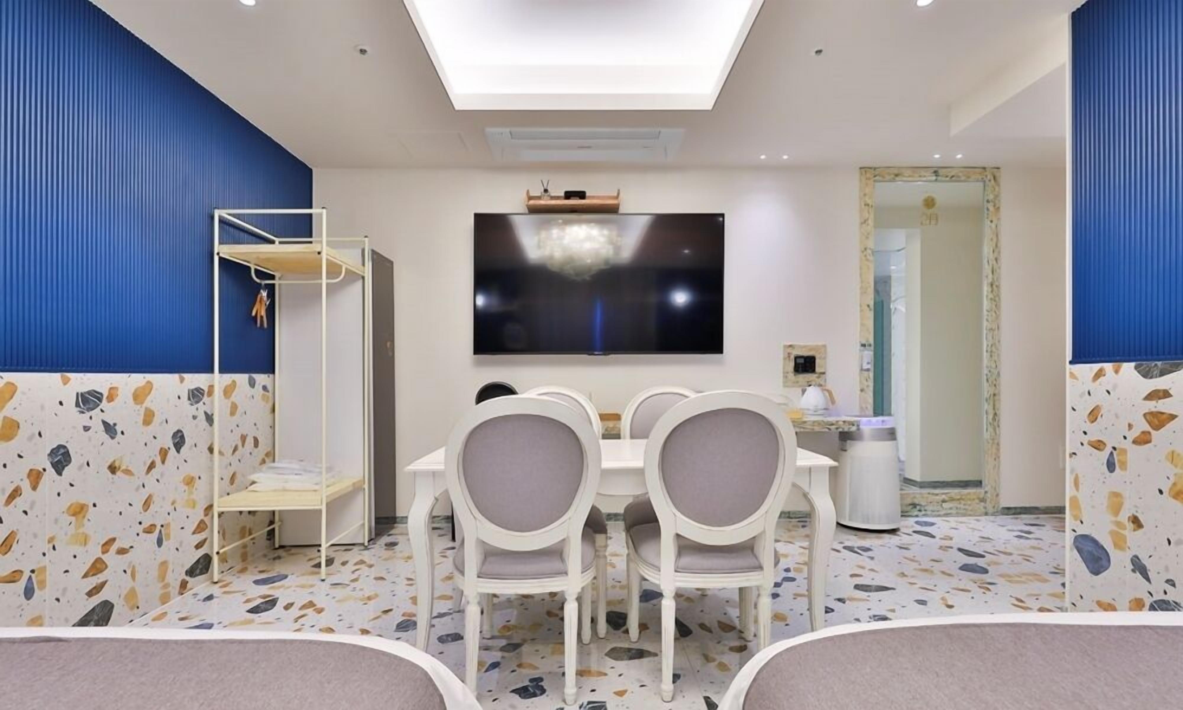 Quarto moderno com televisão, uma mesa de jantar com cadeiras e uma pequena estante.