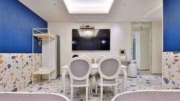 Quarto moderno com televisão, uma mesa de jantar com cadeiras e uma pequena estante.