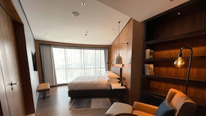 Quarto de hotel moderno com uma cama grande, um sofá, uma mesinha e uma estante.