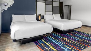 Quarto de hotel moderno com duas camas, um tapete colorido estampado e uma obra de arte original na parede.