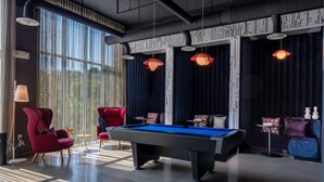 Quarto moderno com mesa de bilhar, cadeiras vermelhas e uma grande janela com cortinas.