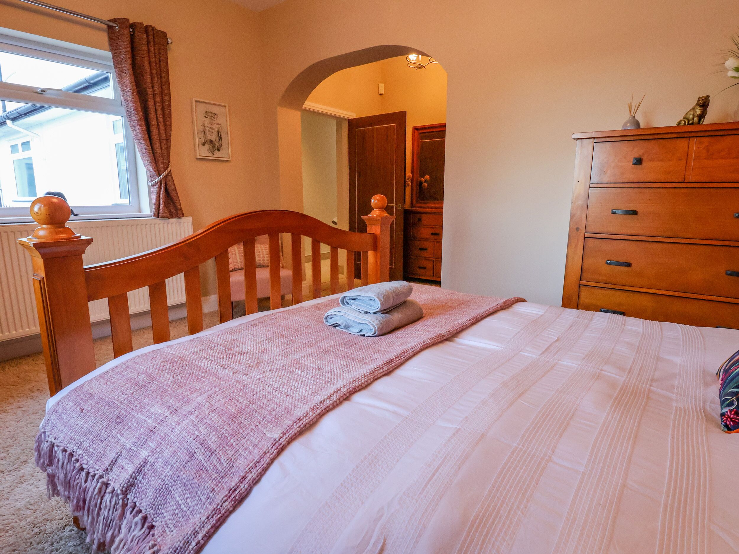 Quarto com cama de madeira, cômoda e janela com cortinas.