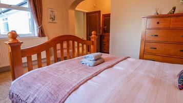 Quarto com cama de madeira, cômoda e janela com cortinas.