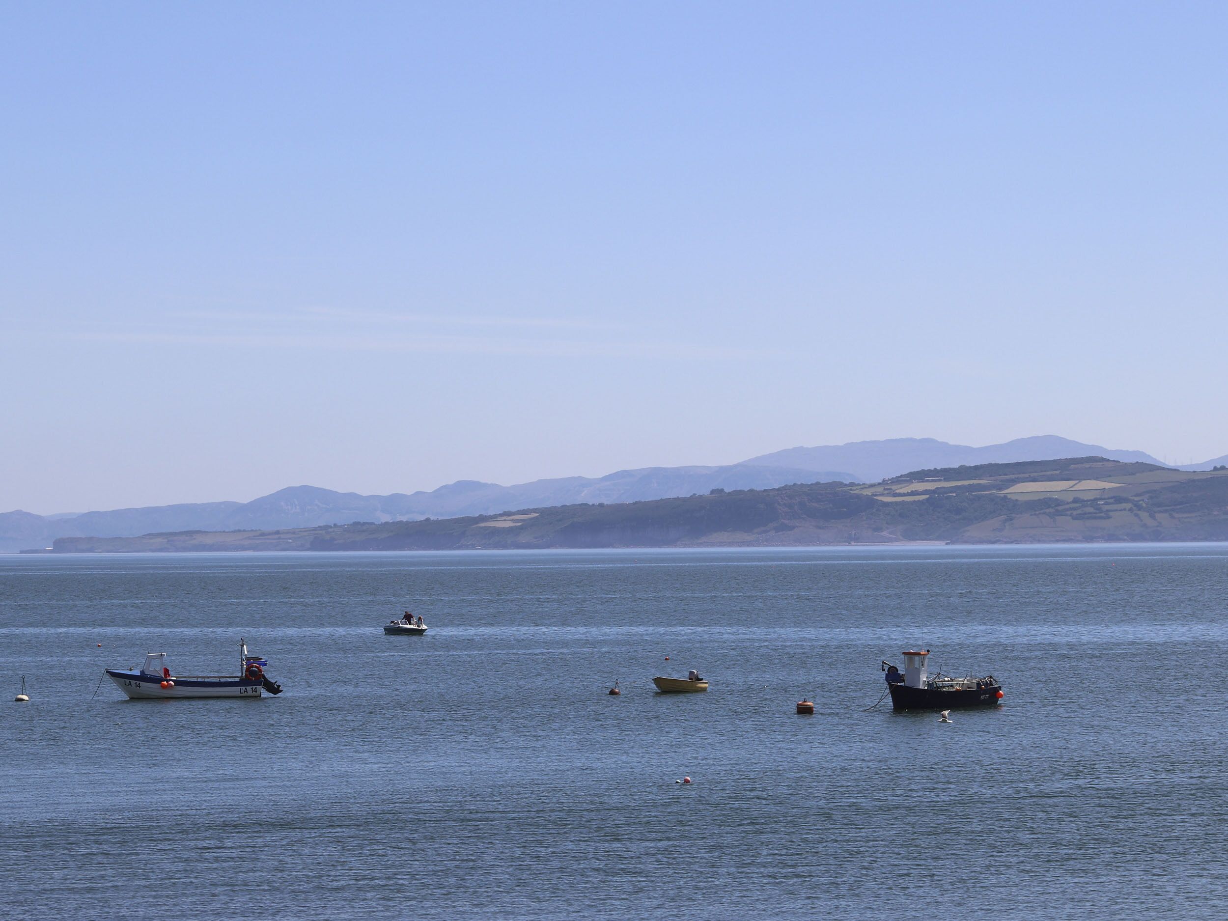 Mar calmo com vários barcos e um farol ao longe.