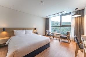 Quarto de hotel moderno com uma cama grande, uma escrivaninha, duas cadeiras e vista para o exterior.