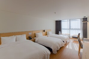 Quarto de hotel com três camas, cabeceira de madeira, uma escrivaninha e uma cadeira.