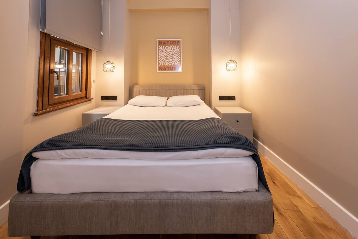 Quarto com cama, mesas de cabeceira, janela e uma obra de arte na parede.