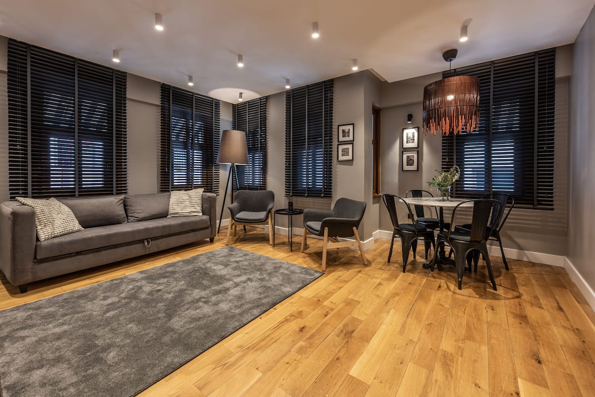 Uma sala de estar moderna com um sofá cinzento, uma mesa de centro e um espaço de jantar com cadeiras.