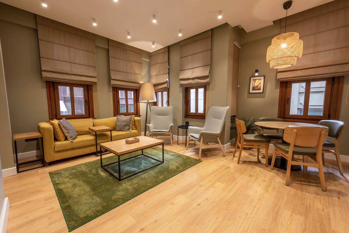 Uma sala de estar espaçosa com um sofá amarelo, uma mesa de centro e um espaço de refeições com cadeiras e uma mesa.