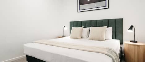 Quarto bem arrumado com uma cama grande, duas mesas de cabeceira, uma cabeceira e uma moldura com uma imagem na parede.