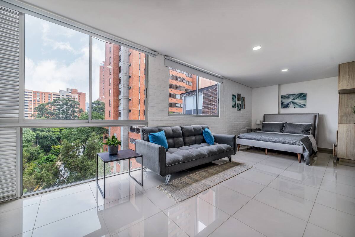 Uma sala de estar moderna com um sofá cinza, uma cama e uma janela grande com vista para a cidade.