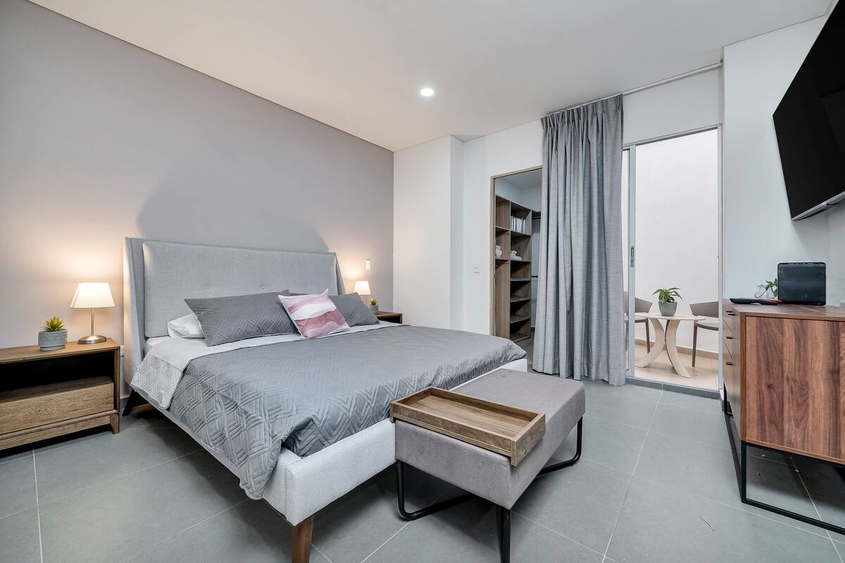 Quarto moderno com cama, mesa de cabeceira, abajur e uma pequena planta.