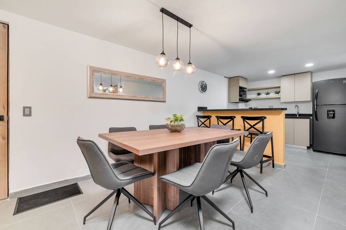 Uma cozinha moderna com uma mesa de jantar de madeira, cadeiras cinzas e iluminação pendente.