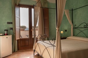 Quarto com cama de dossel, uma mesinha de cabeceira com abajur e vista através de uma porta aberta.