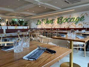 Interior de restaurante com mesas e cadeiras de madeira, e uma parede com a inscrição 'Le Vent Bocage'.