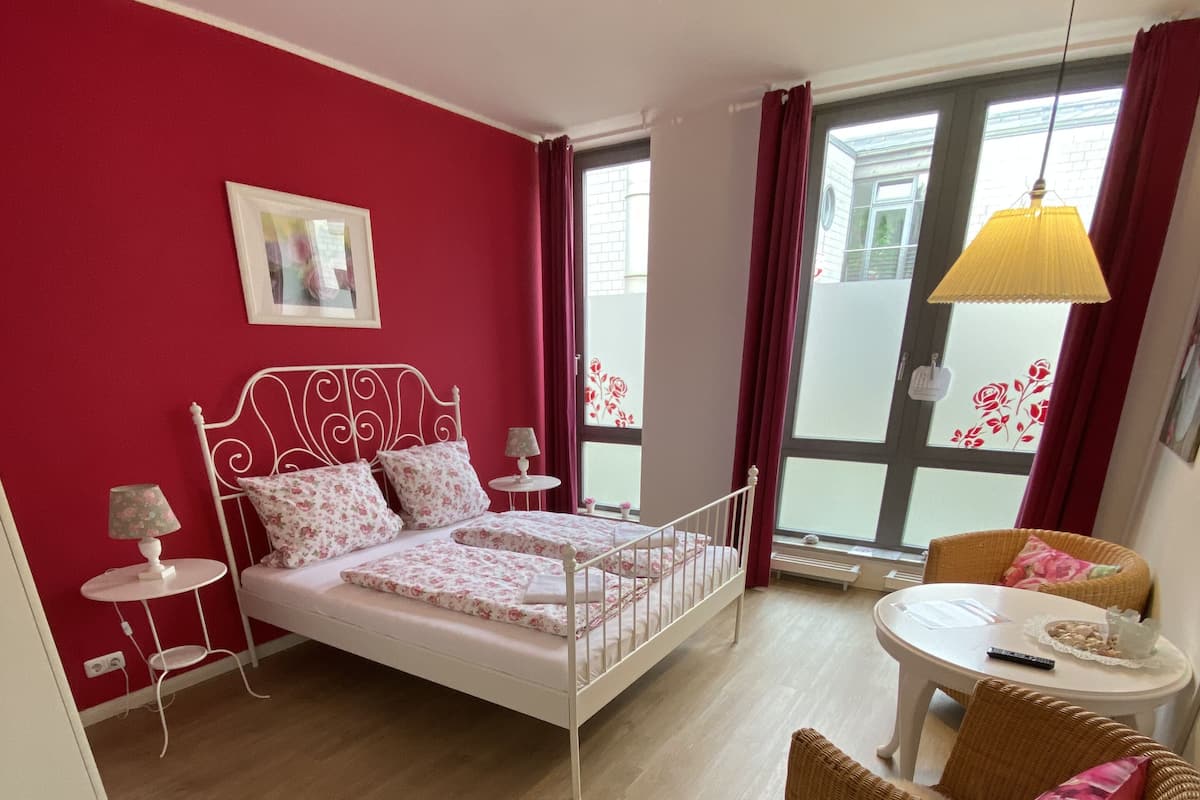 Quarto com cama, uma mesa pequena, cadeira e janela com cortinas.