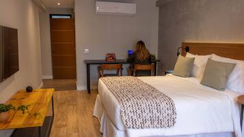 Quarto de hotel com cama, mesa de cabeceira, escrivaninha e cadeira.