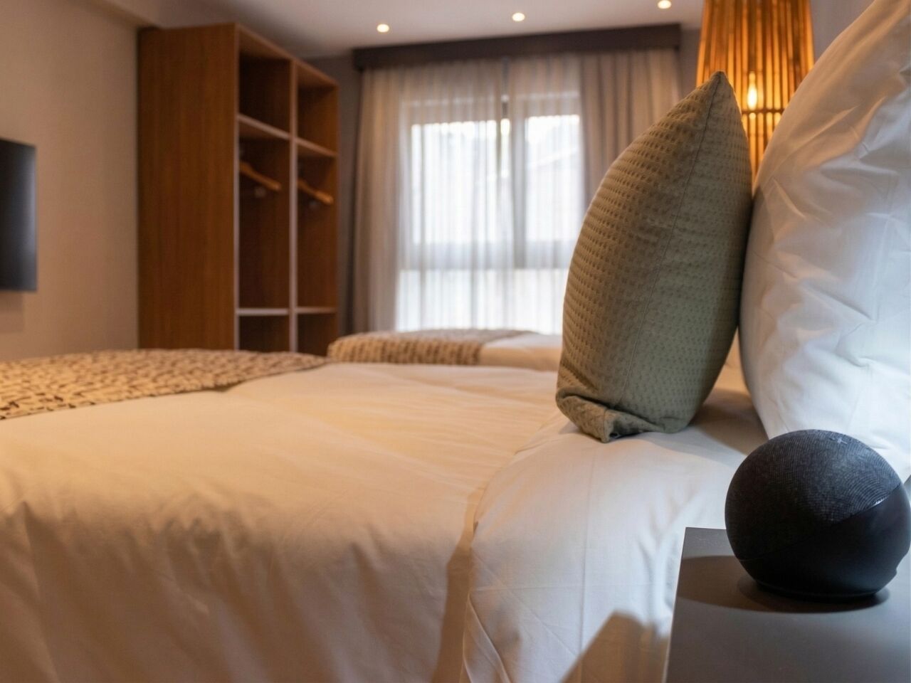Cama bem arrumada com almofadas, mesa de cabeceira com objeto esférico e guarda-roupa em um quarto bem iluminado.