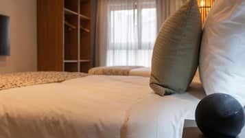 Cama bem arrumada com almofadas, mesa de cabeceira com objeto esférico e guarda-roupa em um quarto bem iluminado.
