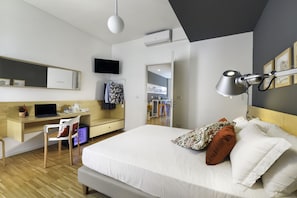 Quarto de hotel moderno com cama, escrivaninha, cadeira e televisão fixada na parede.