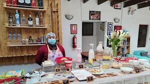 Um café com diversos tipos de bebidas e comidas expostas em uma mesa, uma seleção de chás, e uma pessoa atrás do balcão.