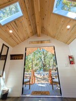 Uma cabana de madeira com telhado inclinado, porta que dá para um deck externo e um extintor de incêndio fixado na parede.