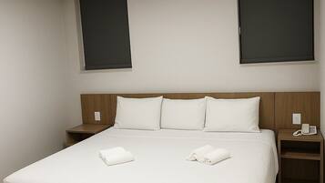 Quarto de hotel com uma cama grande, duas mesas de cabeceira, uma televisão de tela plana na parede e uma luminária no teto.