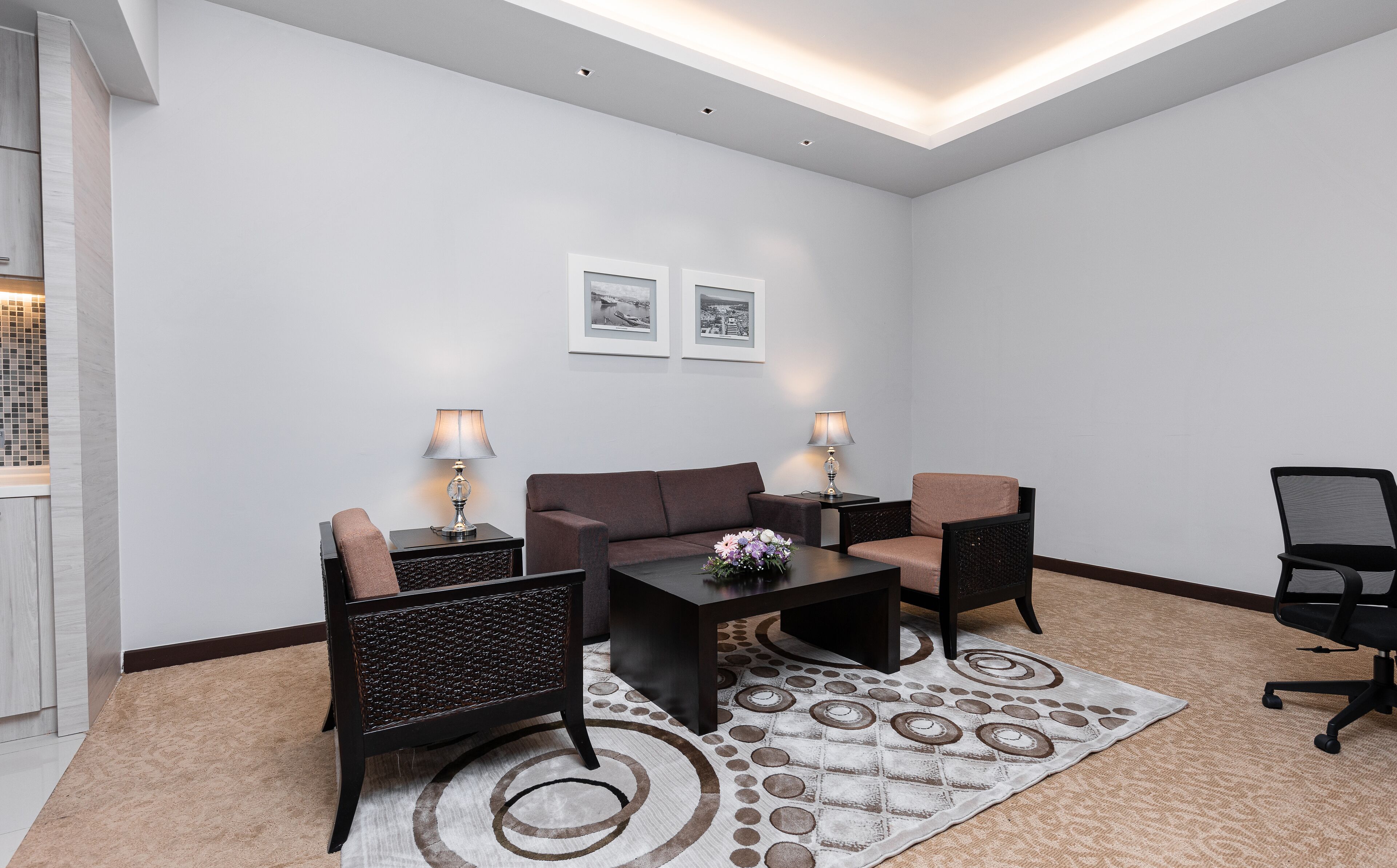 Quarto moderno com sofá, duas poltronas, mesa de centro e tapete. Há duas luminárias em mesas laterais e duas quadros na parede.